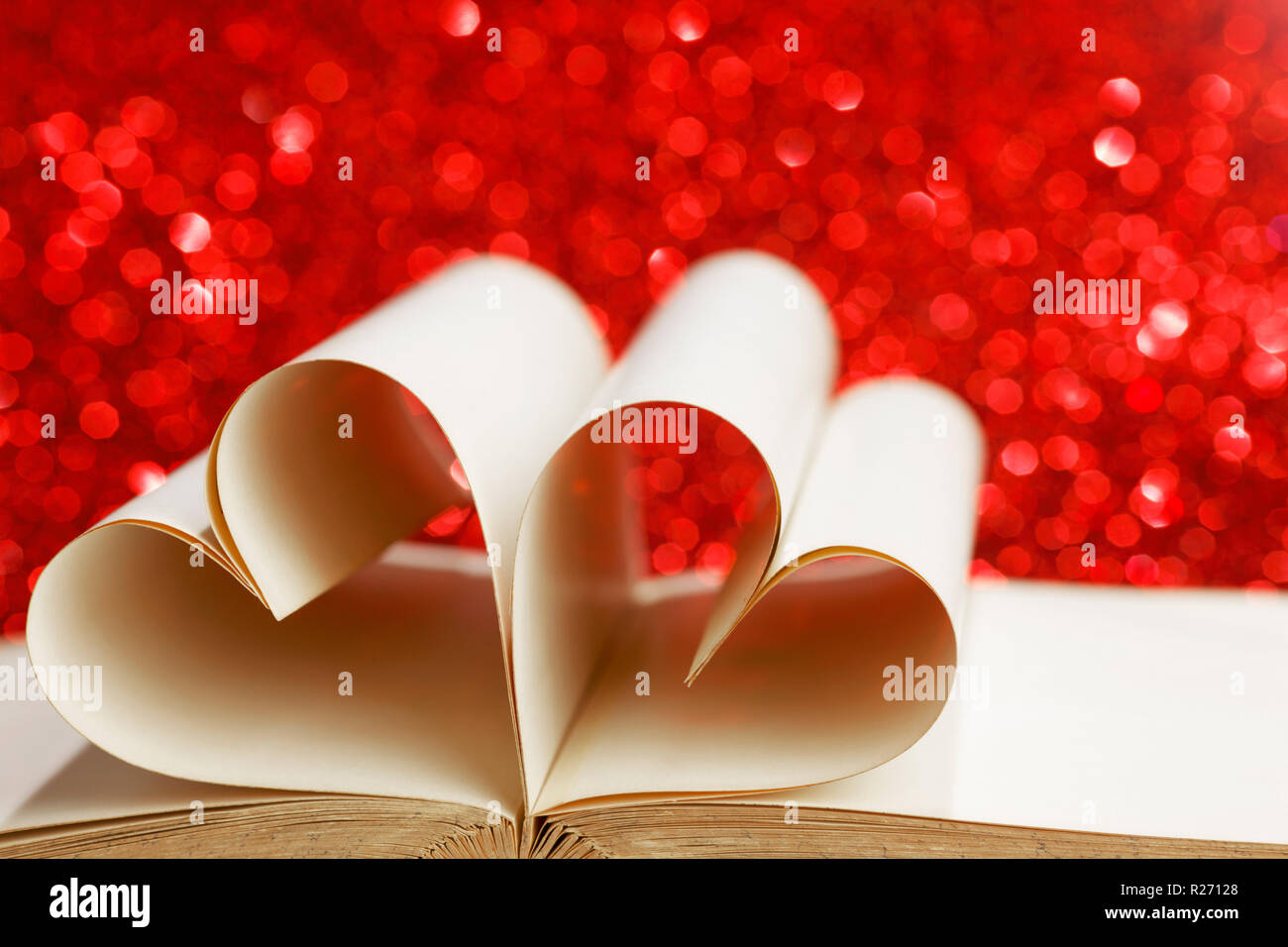 Pages of open book rolled in heart shape on glitter background Stock ...