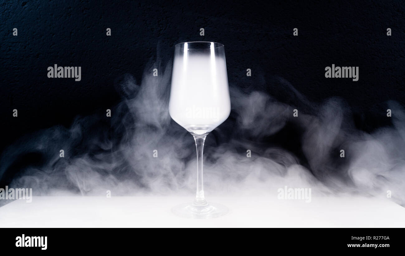 wine glas filled with smoke on a white table with a black background ...