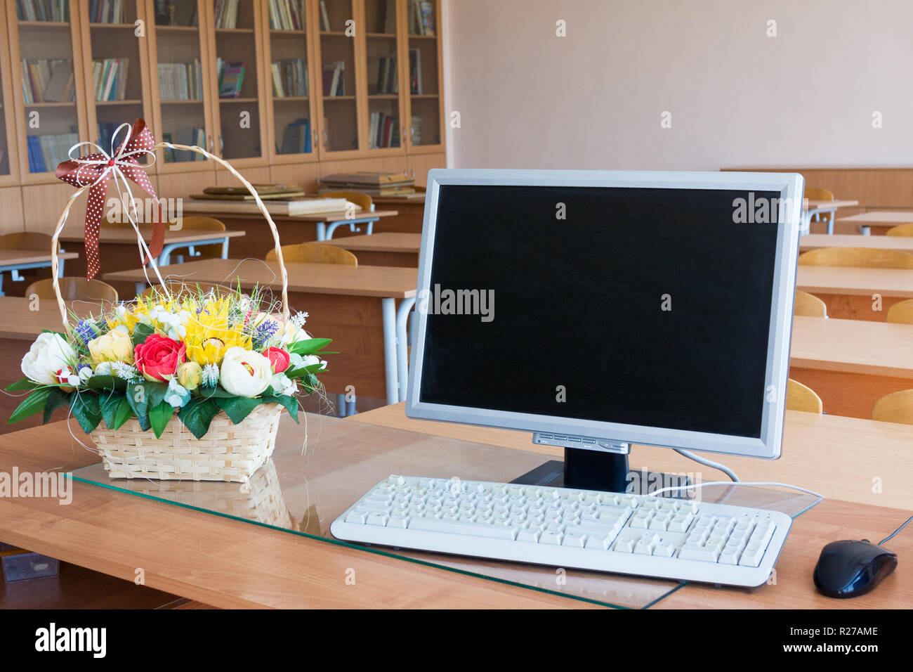 Basket with paper flowers and computer on teacher`s table in classroom ...