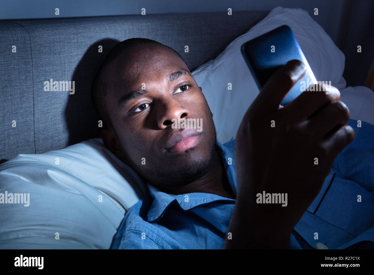 African Man Lying On Bed Using Mobile Phone At Night Stock Photo - Alamy