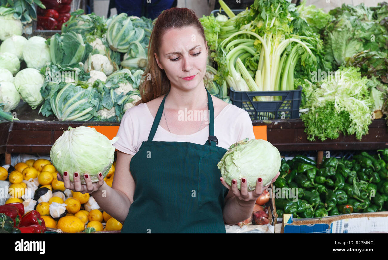 adult seller is holding green cabbage on her workplace in the market ...