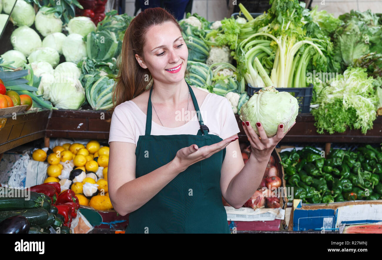Portrait of positive seller woman who is holding cabbage in the ...