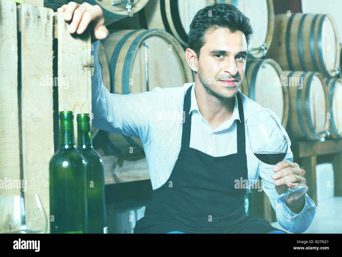 Smiling positive man in uniform having glass with wine sample in ...