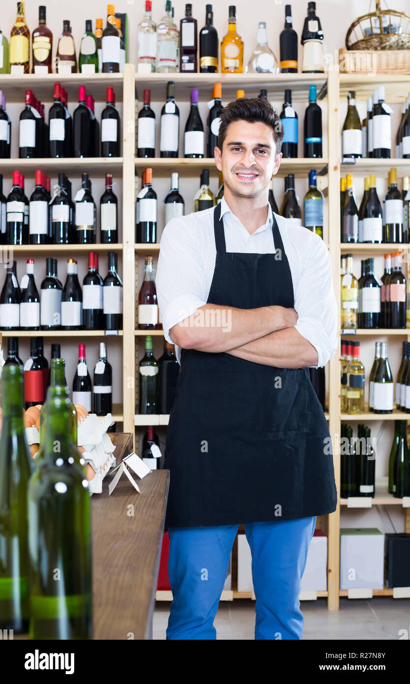 Smiling russian man seller wearing uniform standing in shop with wine ...