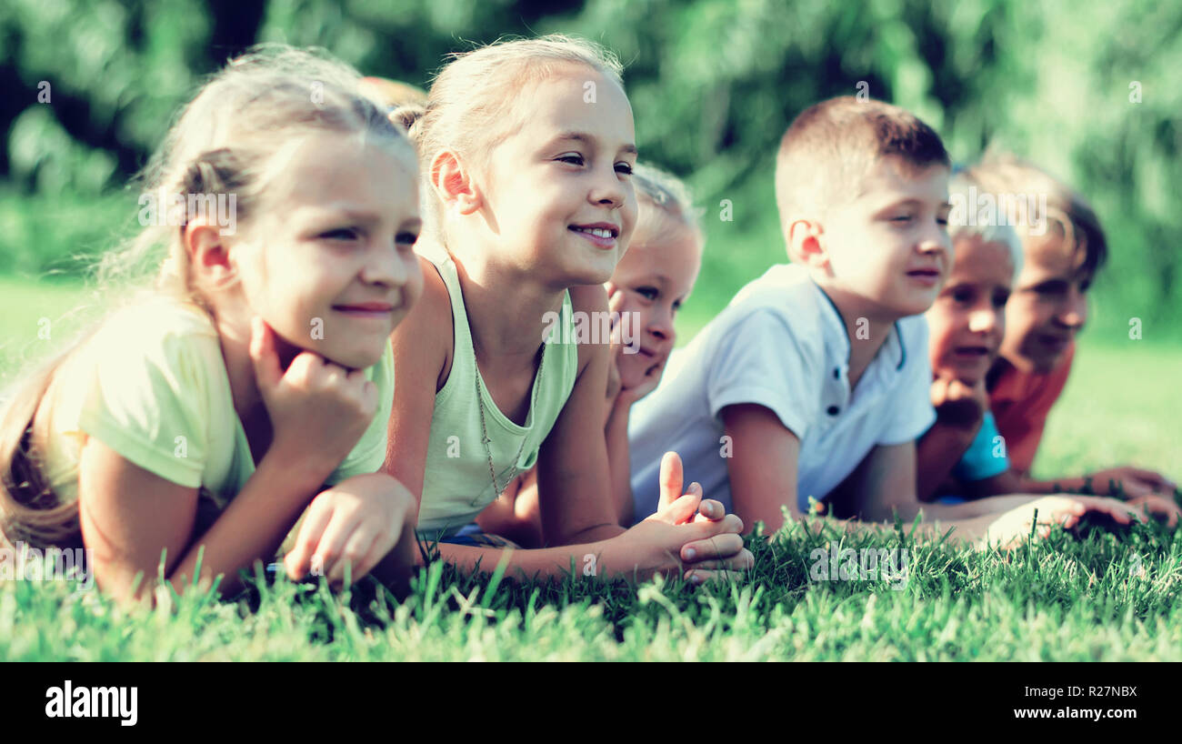 portrait of smiling children lying on grass in park and looking happy ...