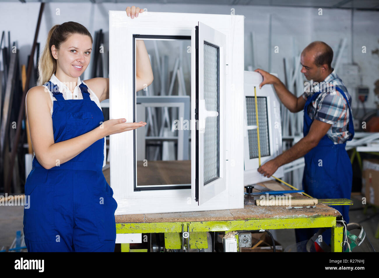 Portrait of craftswoman in blue overalls demonstrating finished plastic ...