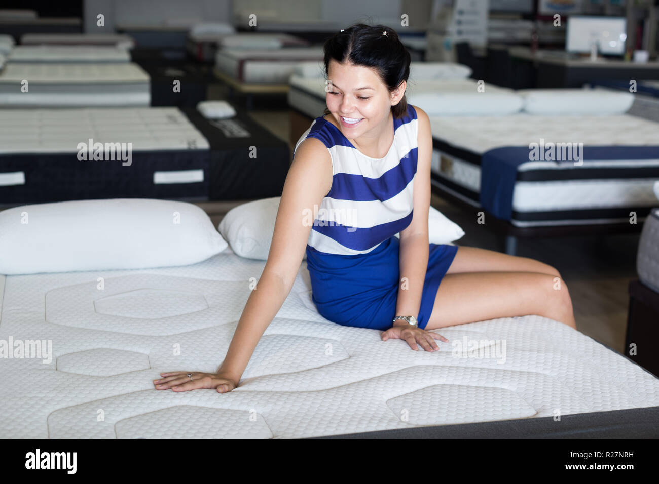 Customer smiling girl is sitting testing new mattress before buying it ...