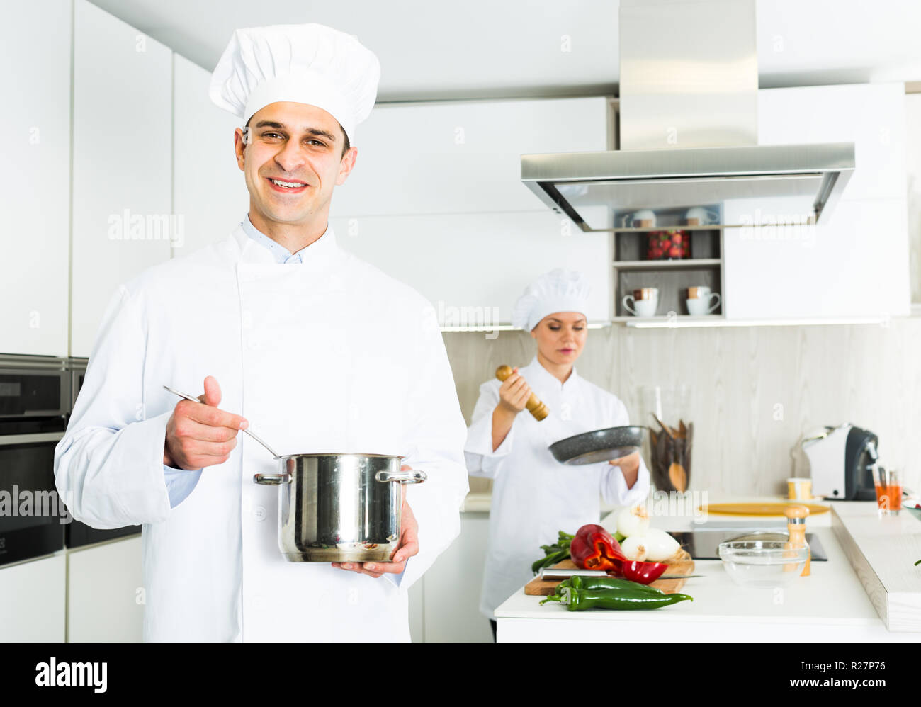 Male cook wearing uniform with stewpot working on kitchen with woman ...