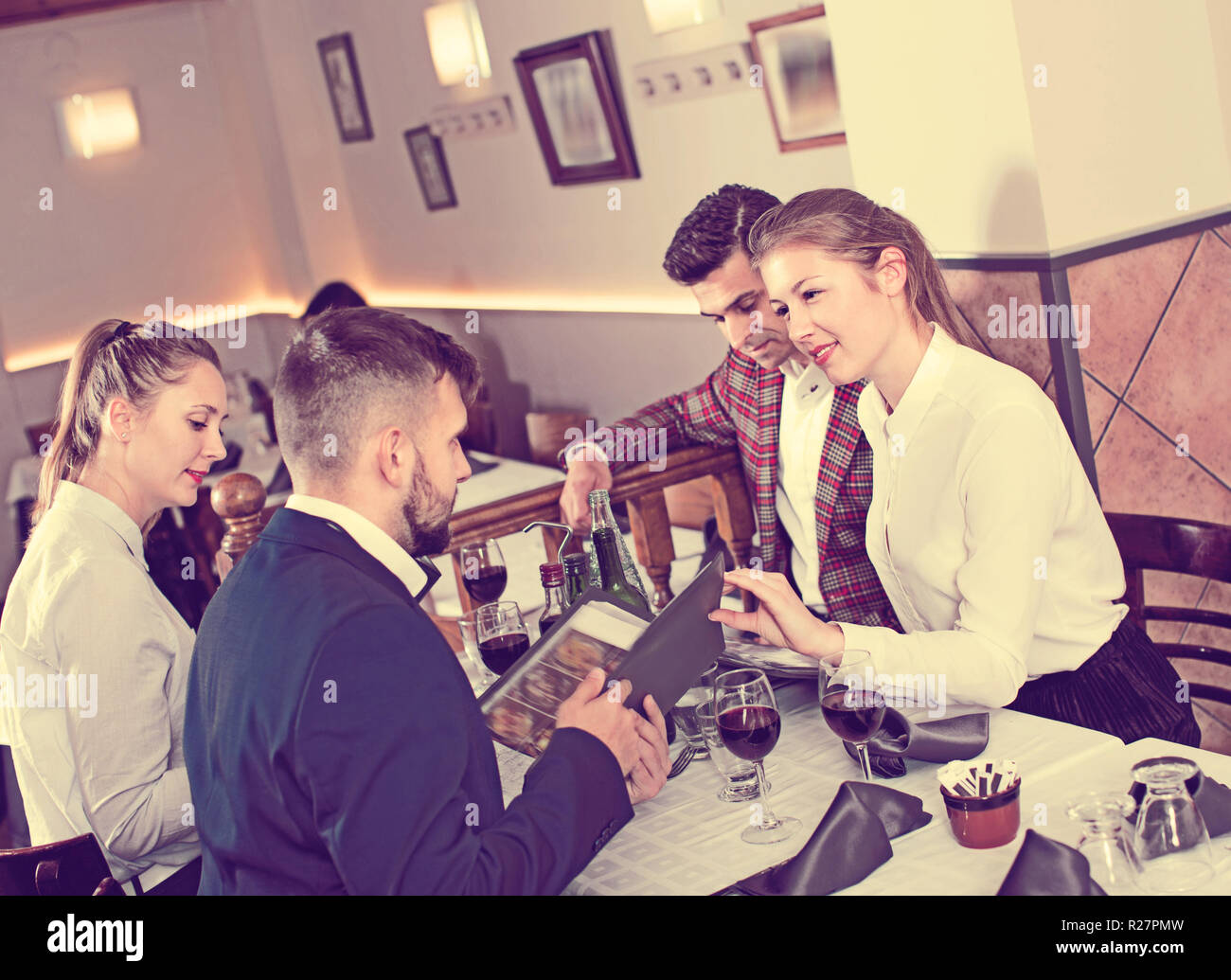 Ð¡heerful positive smiling friends choosing dishes out of menu card in ...