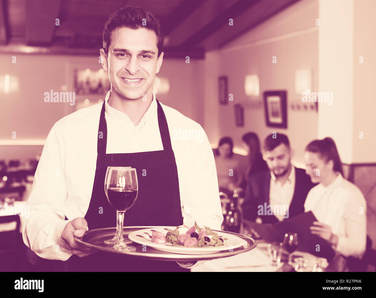 Polite waiter holding serving tray at restaurant with customers his ...