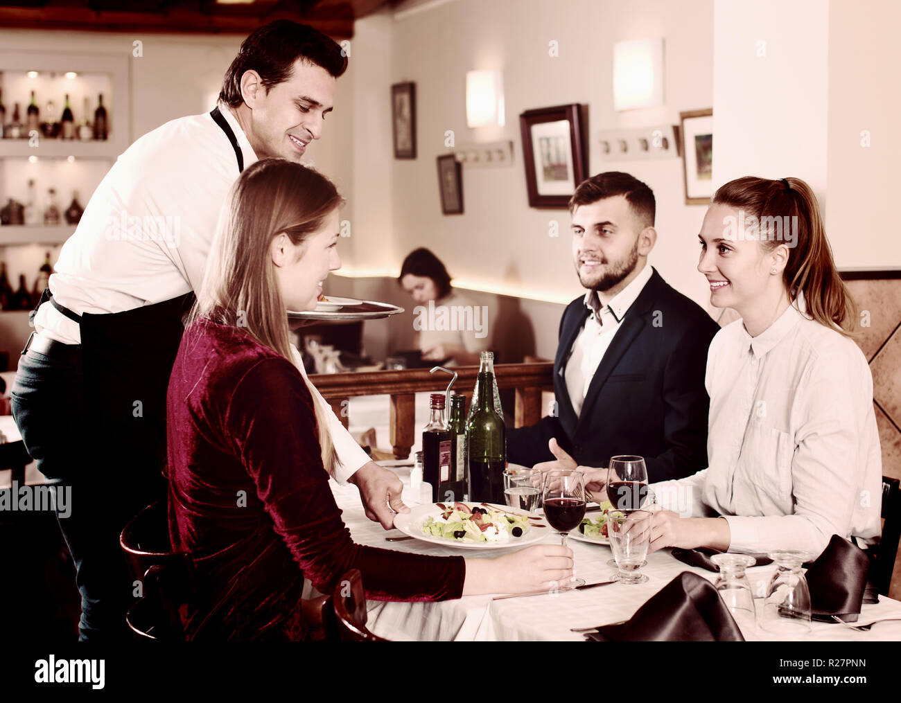 Polite cheerful waiter bringing ordered dishes to guests at restaurant ...