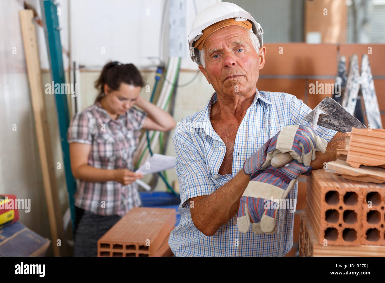 Portrait of confident experienced elderly builder mason near red brick ...