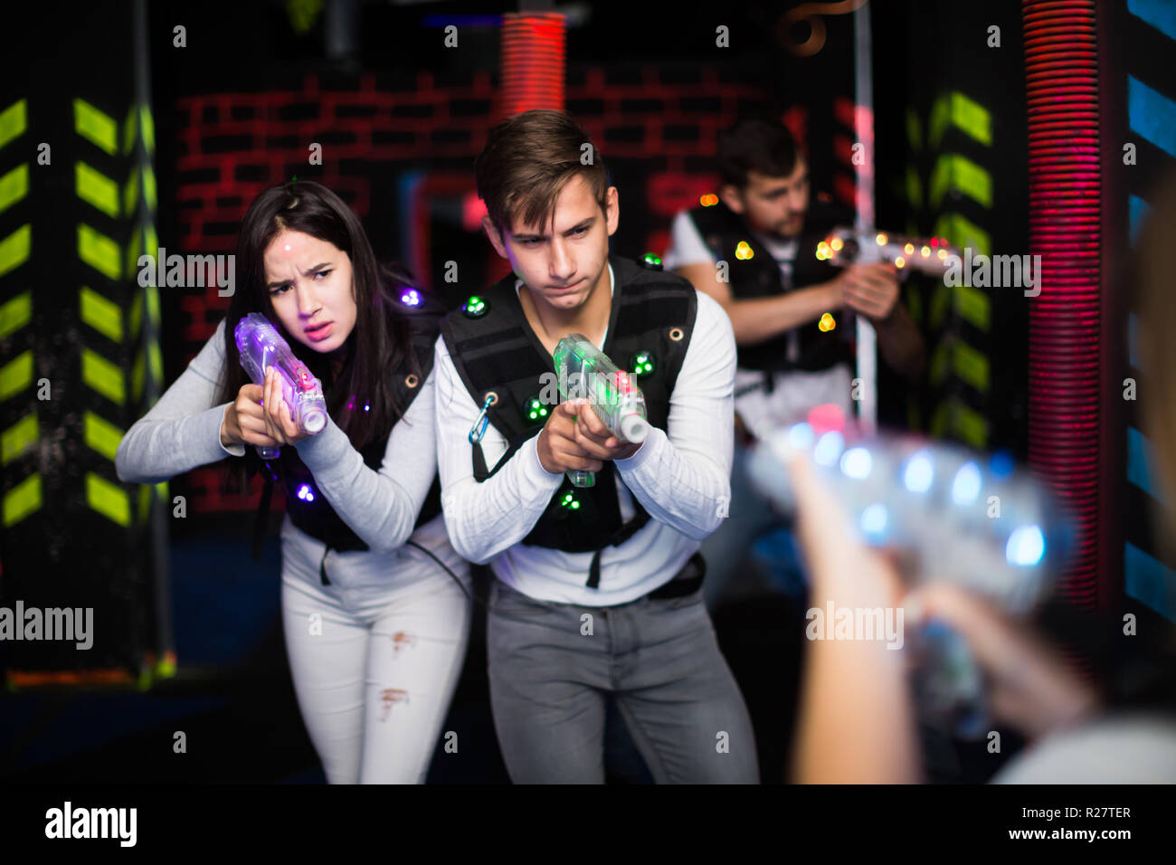 Modern guy and girl aiming laser guns at other players during laser tag ...