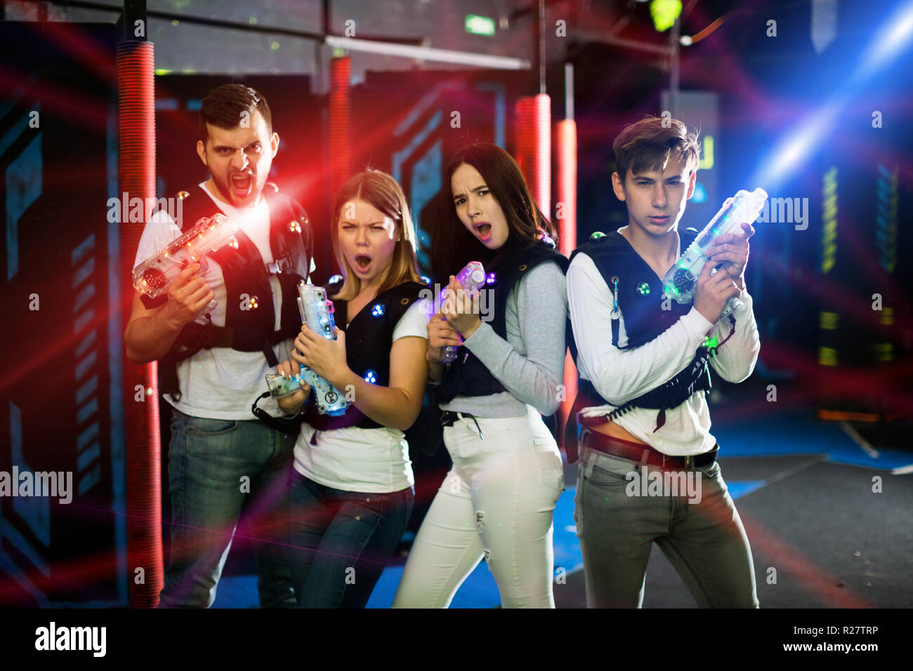 Happy young people with laser pistols posing together in bright beams ...