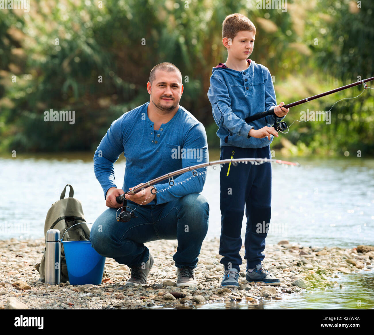 Portrait of happy glad father and son fishing with rods in summer day ...