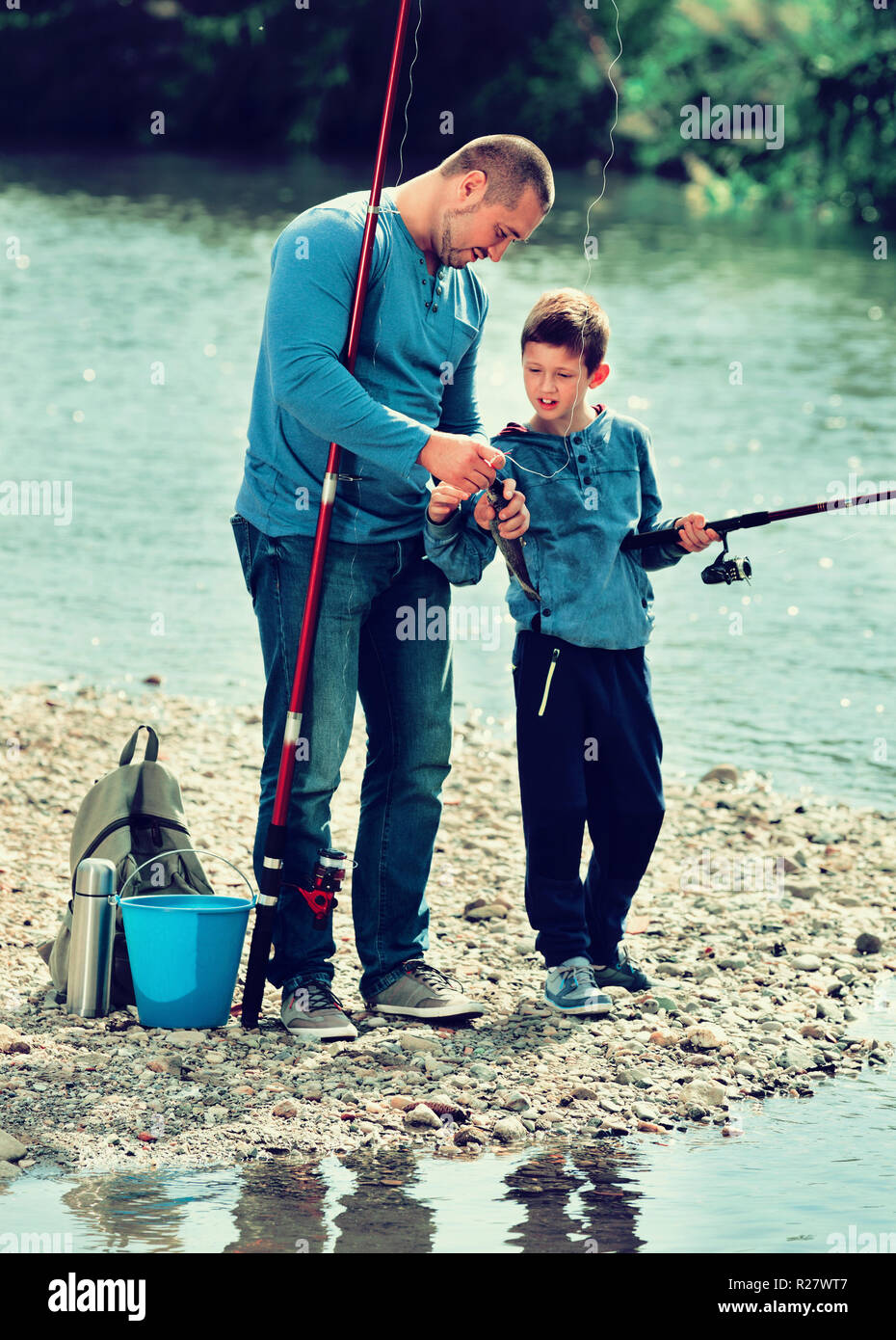 Portrait of smiling father and cute son fishing with rods in summer day ...