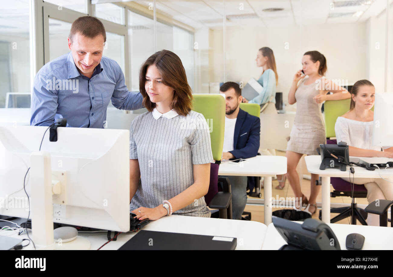 Experienced businessman helping female colleague in work with computer ...