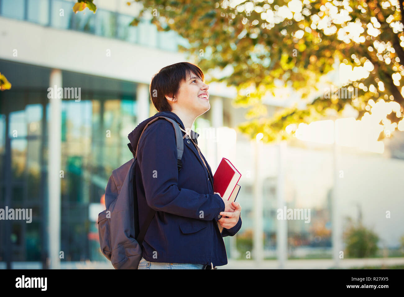 Happy young woman student holding books and backpack outdoors ...