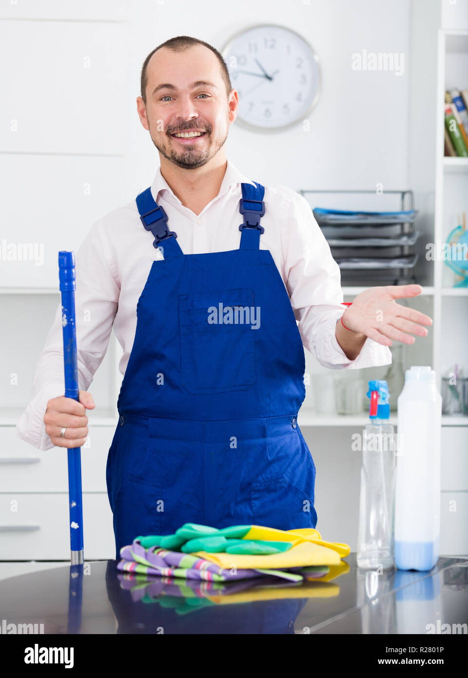 Positive young man in apron cleaning his office desk by cleanser Stock ...