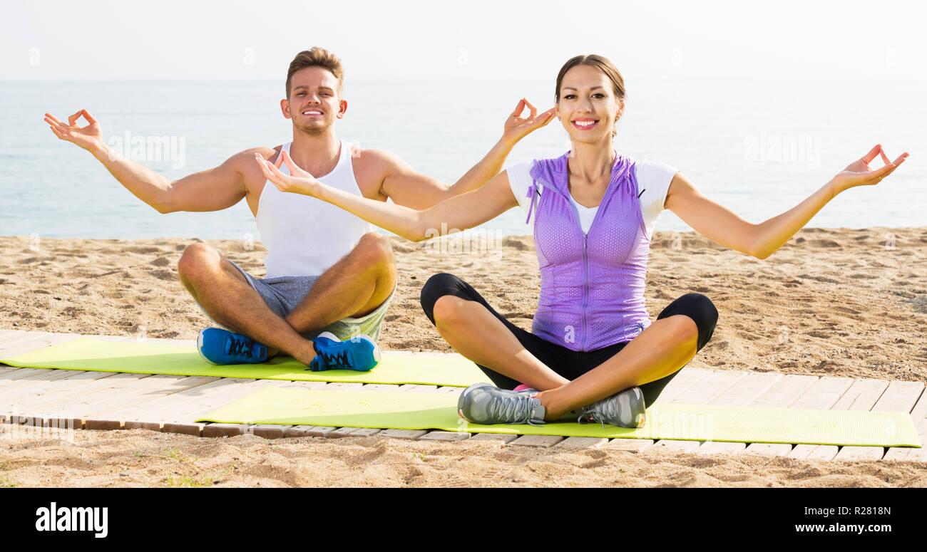 Positive cross-legged guy and girl training yoga poses on seaside Stock ...