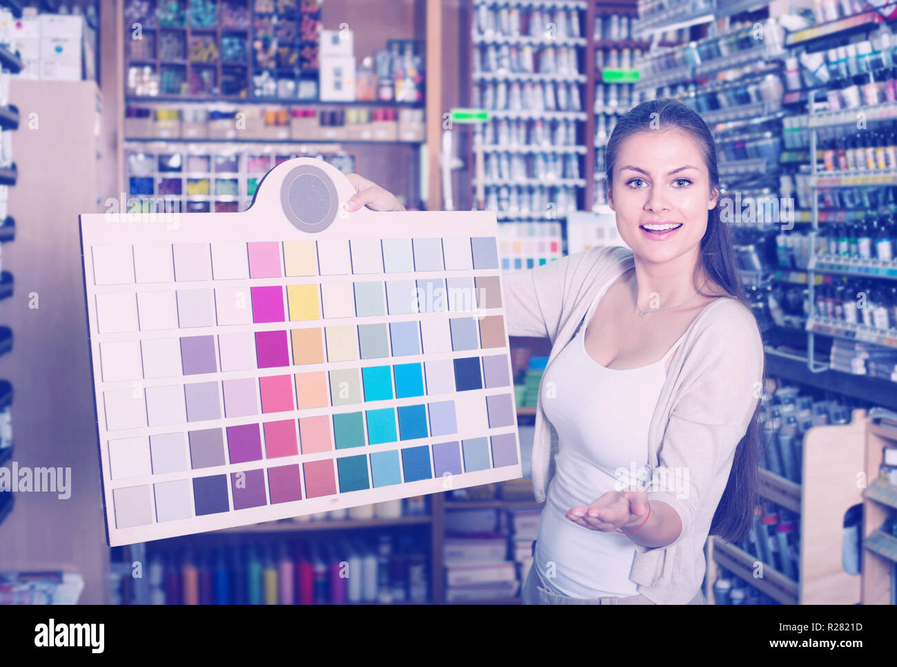 cheerful woman choosing paint color using sample palette in art store ...