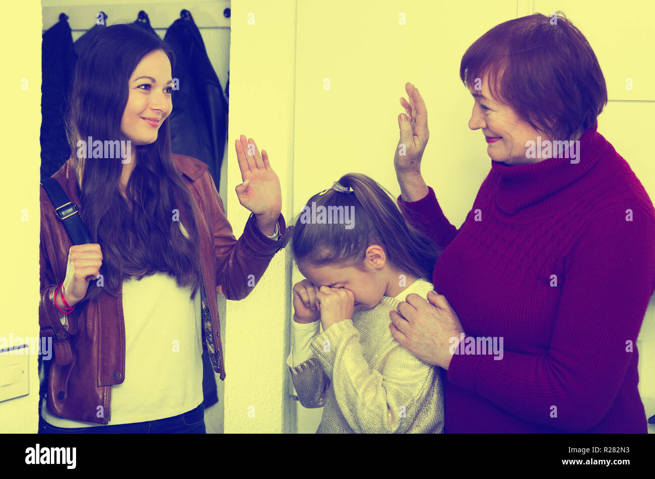 Smiling young mother leaving daughter in tears with grandma at home ...
