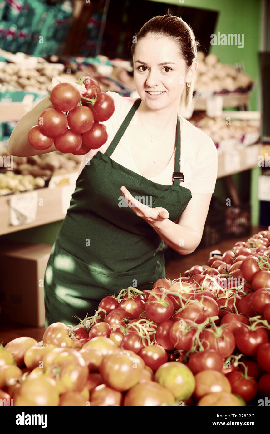Friendly attractive saleswoman offering ripe tomatoes in supermarket ...