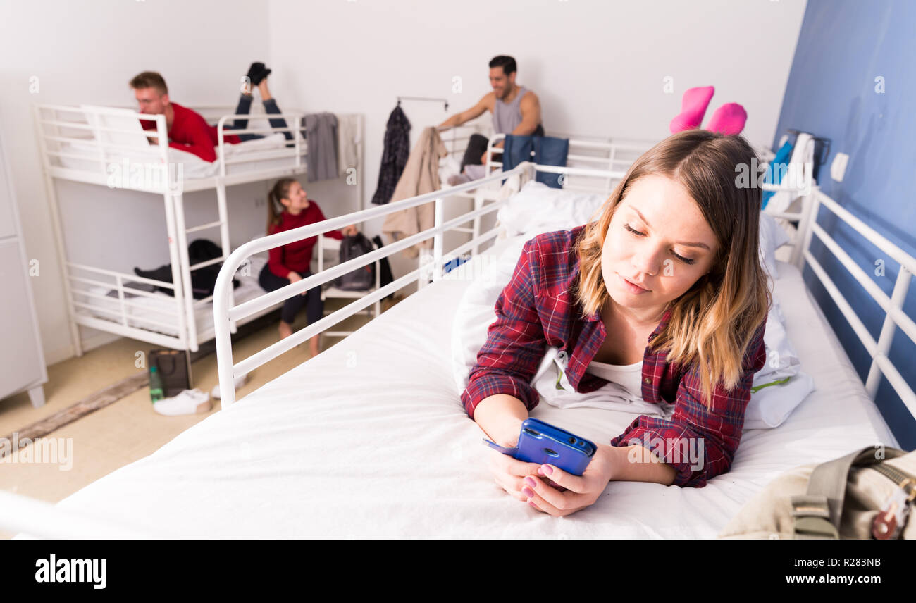 Young woman lying on top bunk of bunk bed in hostel, looking at ...