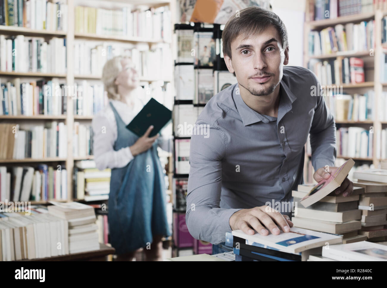 portrait of intelligent young man standing among bookshelves and ...