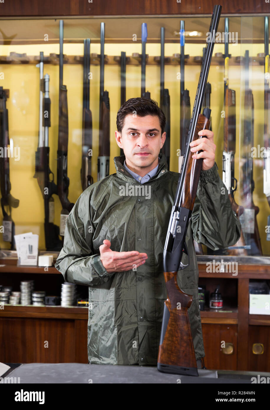 Portrait of handsome confident man in gun shop showing rifle Stock ...