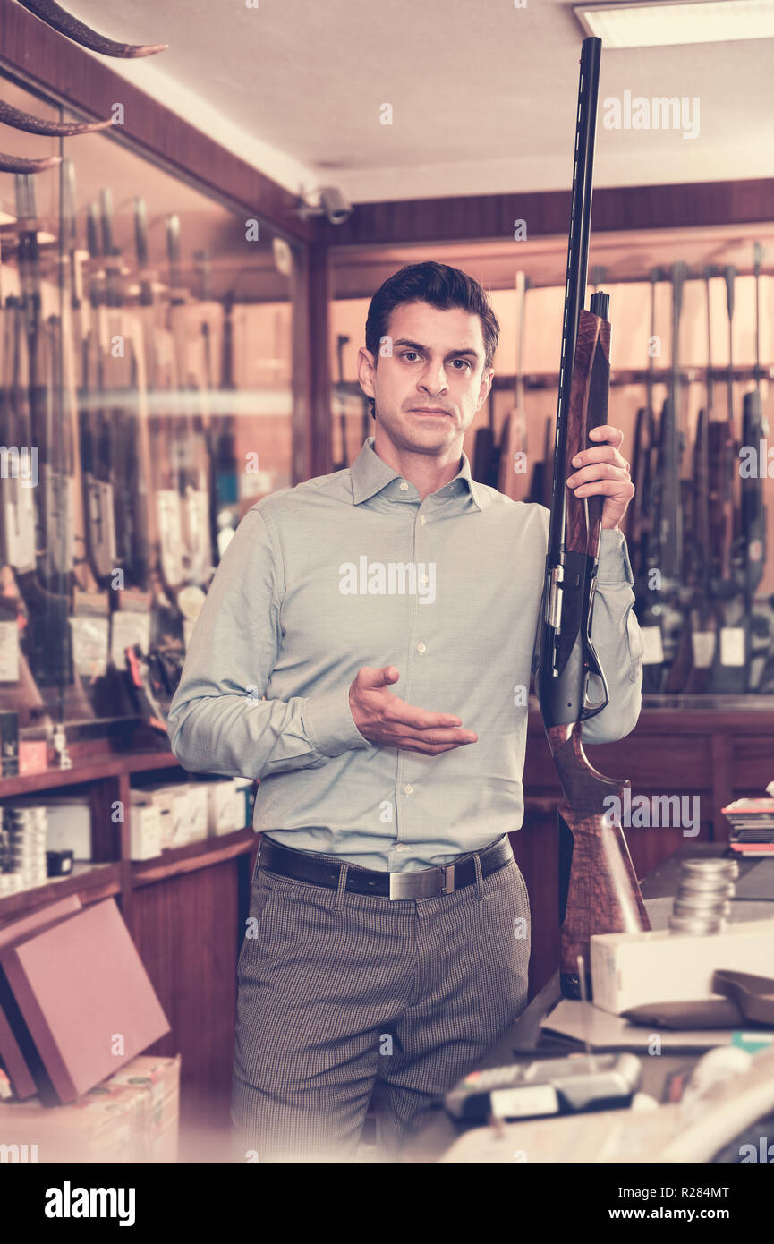 Portrait of positive salesman in gun shop showing rifle Stock Photo - Alamy