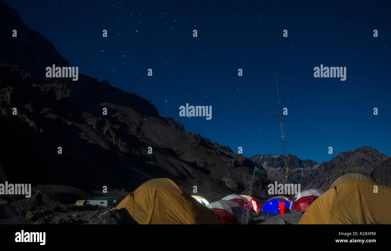 Night view of a camp surrounded by rocky mountains with a starry night ...