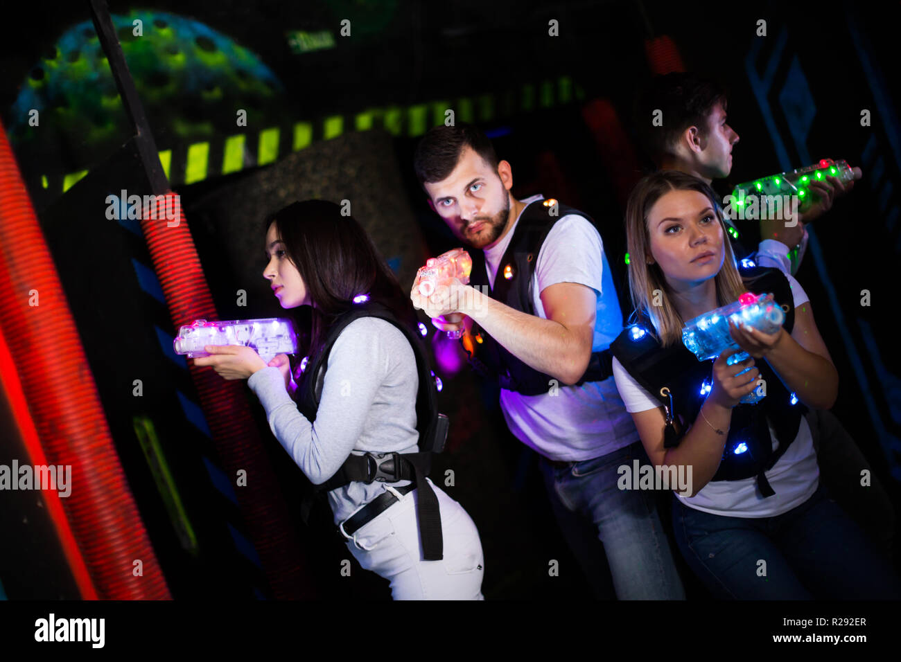 Excited young people aiming laser guns at other players during lasertag ...