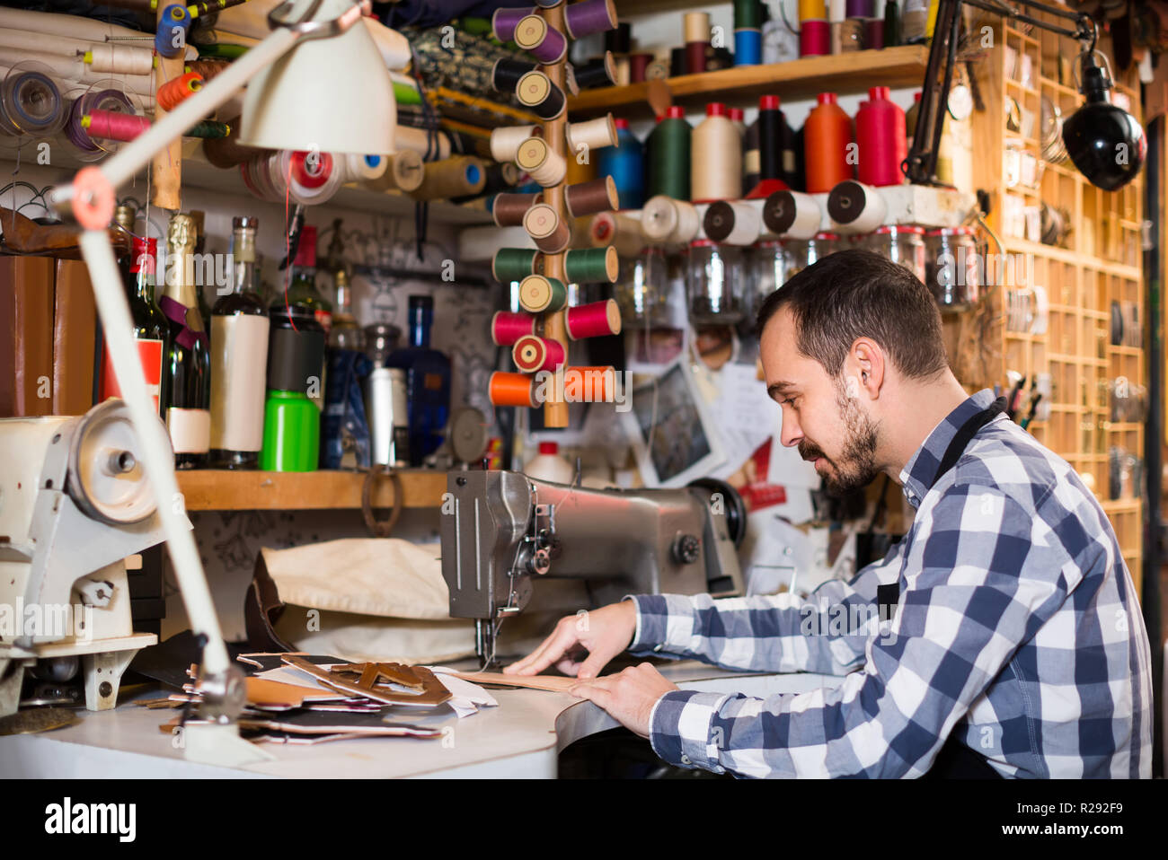 happy european male worker sewing stitches on belt in leather workshop ...