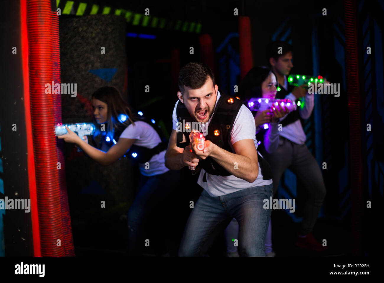 Portrait of young man with laser gun having fun on dark laser tag arena ...