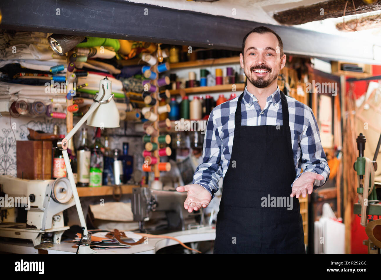 Young male worker demonstrating workplace and tools in leather workshop ...