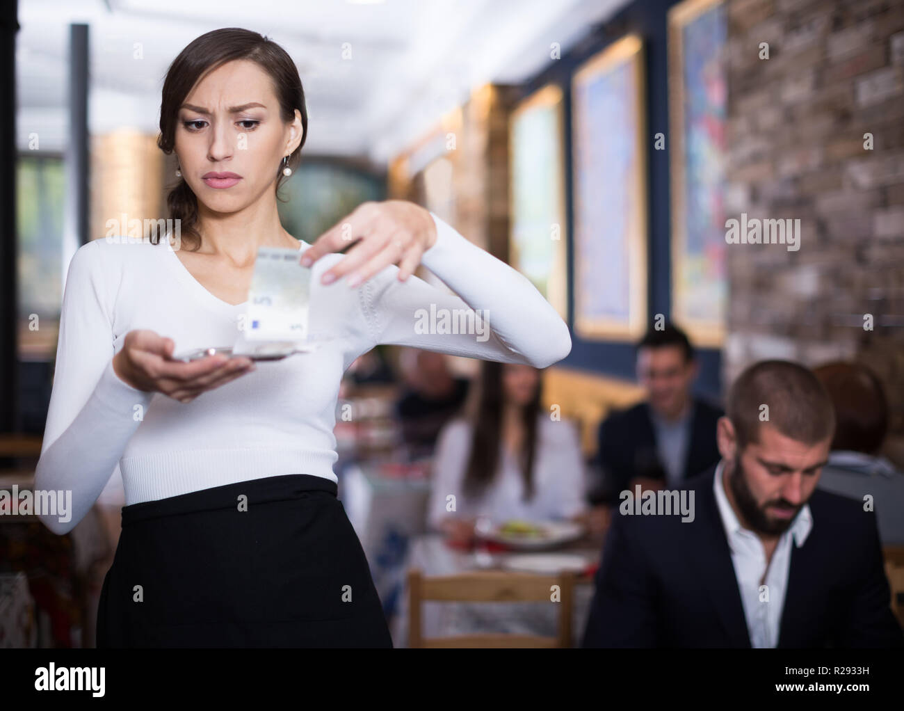 Surprised waitress woman considering a tray with money in a restaurant ...