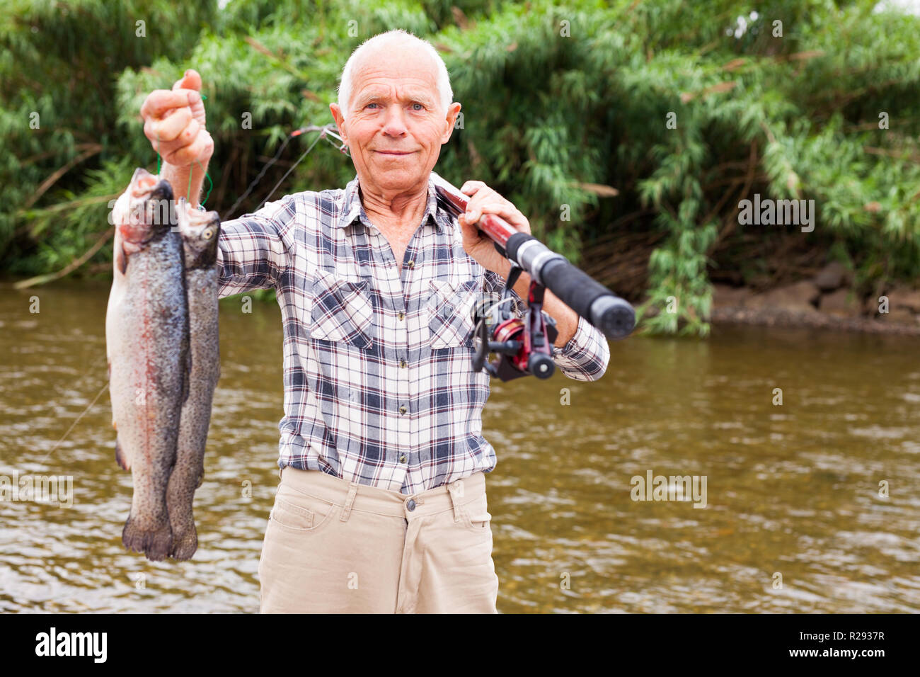 Portrait of smiling mature man holding fresh catch fish and angling ...