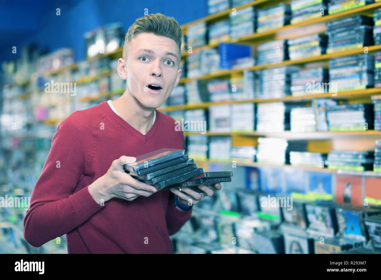 Surprised young man standing in store with stack of DVDs indoors Stock ...