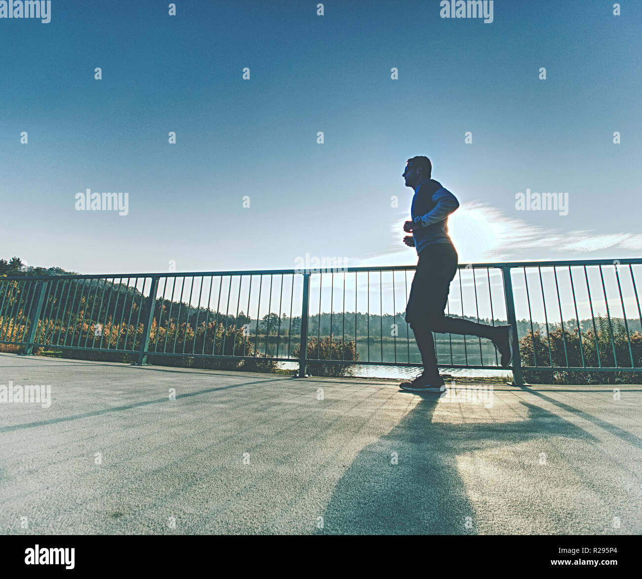 Attractive wiry man jogging against to sun. Regular morning training at sea. Young sportsman ...