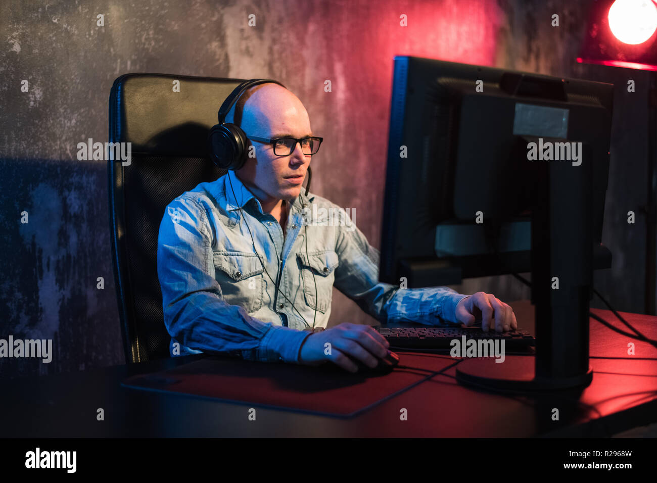 Serious young man sitting and working with computer in dark office ...