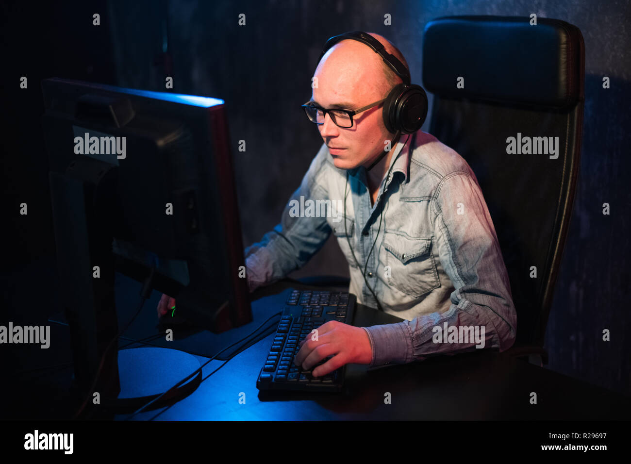 Serious young man sitting and working with computer in dark office ...