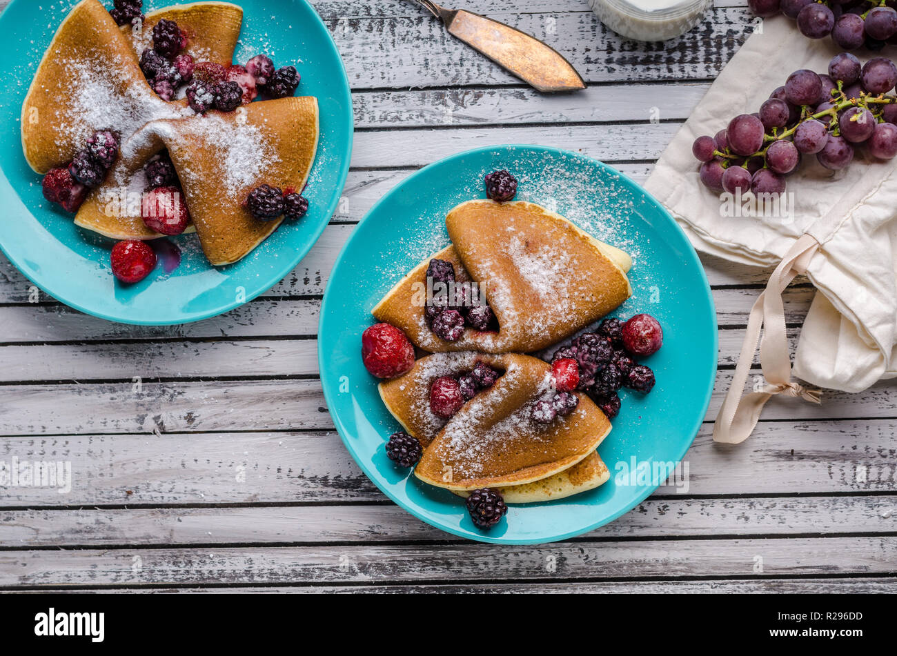 Homemade crepes with frozen berries, topped sugar, rustic wood board ...