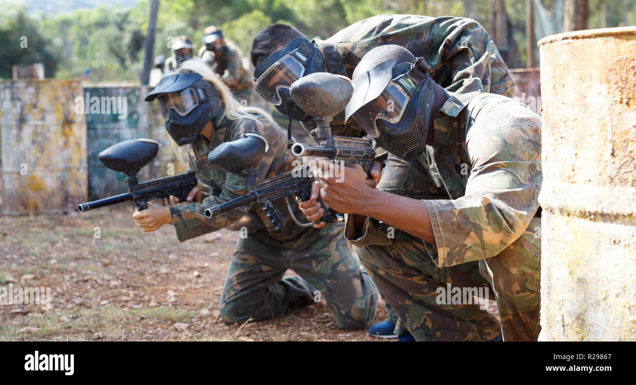 Diligent positive paintball players aiming and shooting with guns at ...