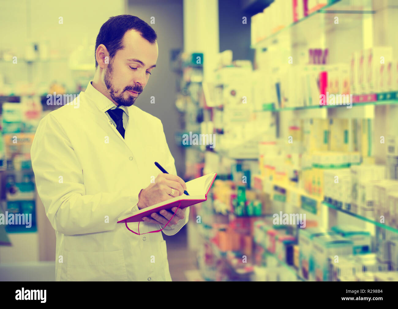 Positive adult man pharmacist writing down assortment of drugs in ...