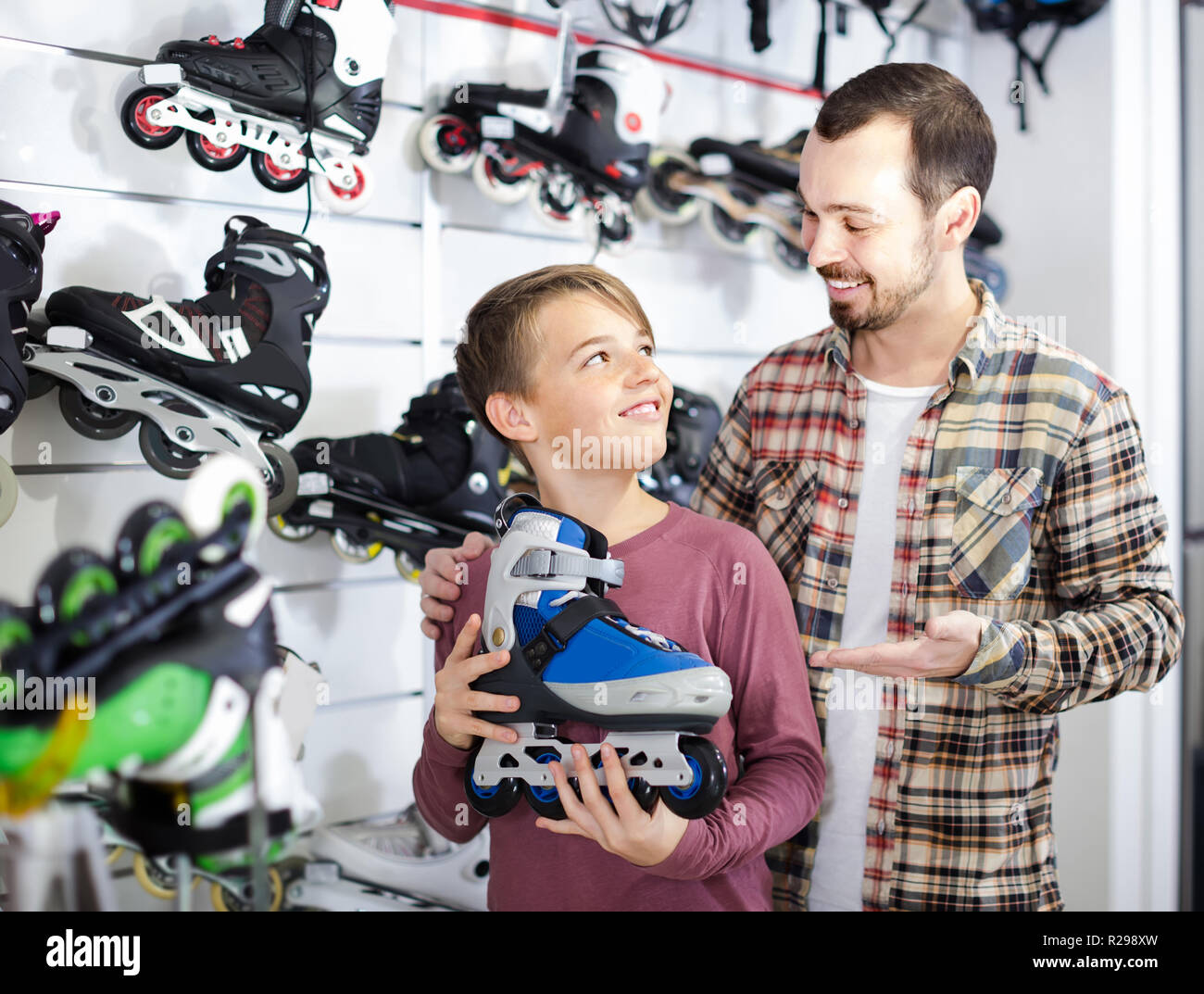 happy russian male shop assistant helping boy to choose roller-skates ...
