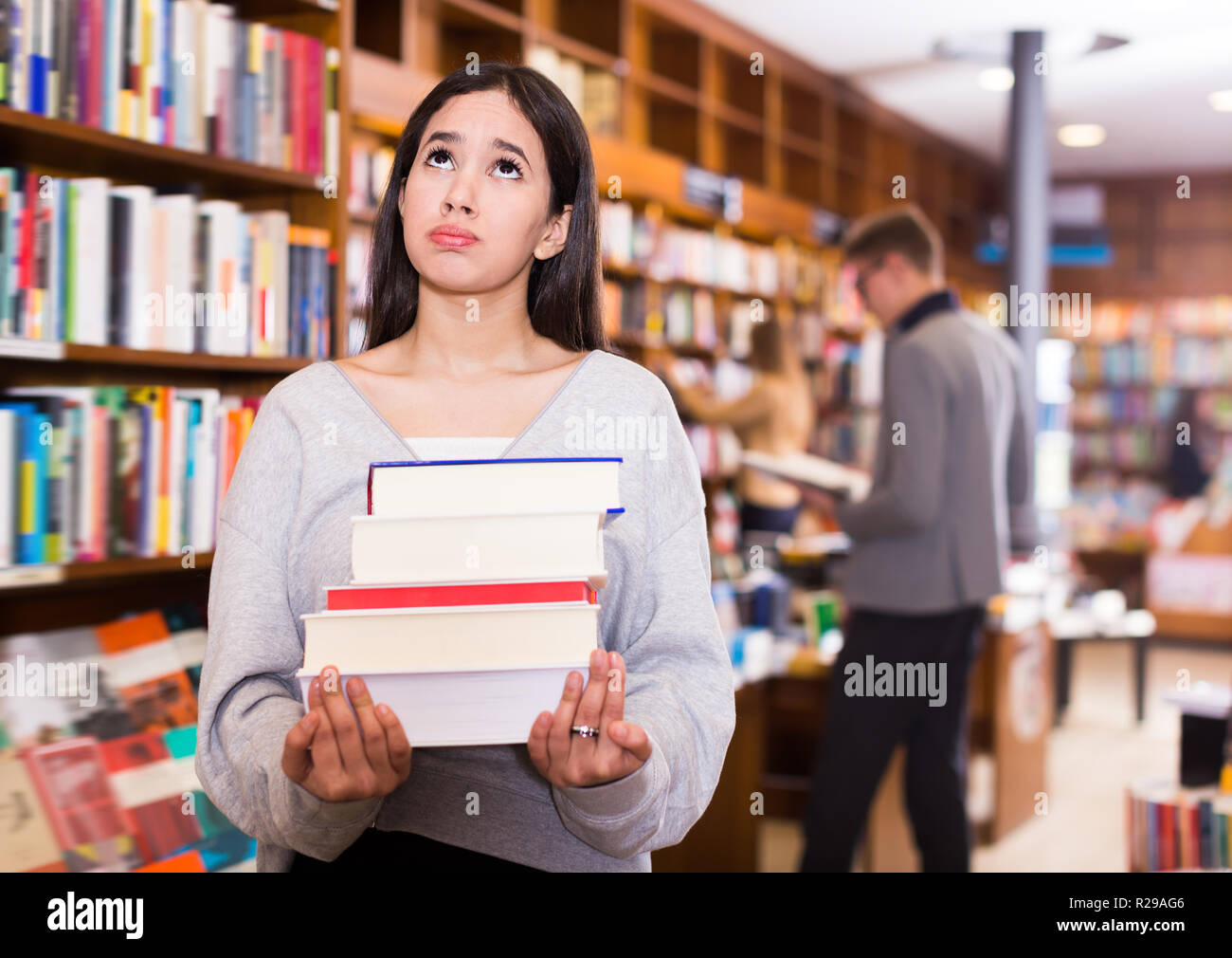 Portrait of weary girl with stack of books in hands in bookshop Stock ...