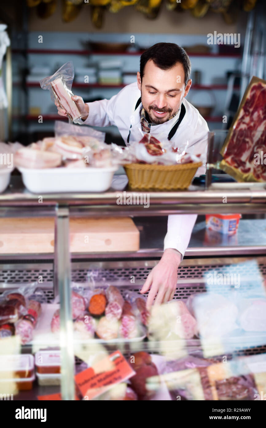 Positive man assistant working with meat in butcher’s shop Stock Photo ...