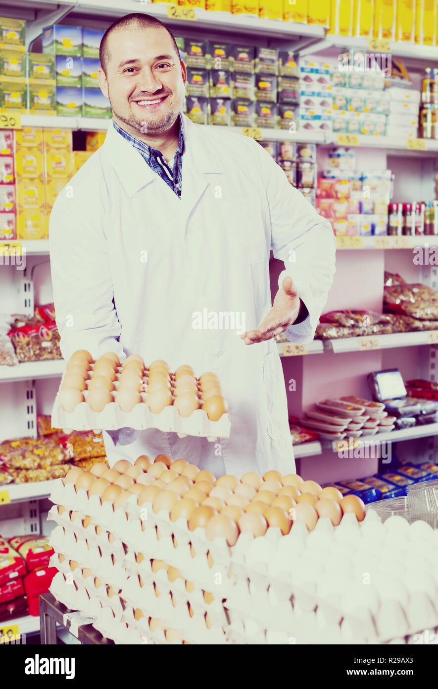 Friendly smiling male staff standing near boxes with eggs in ...