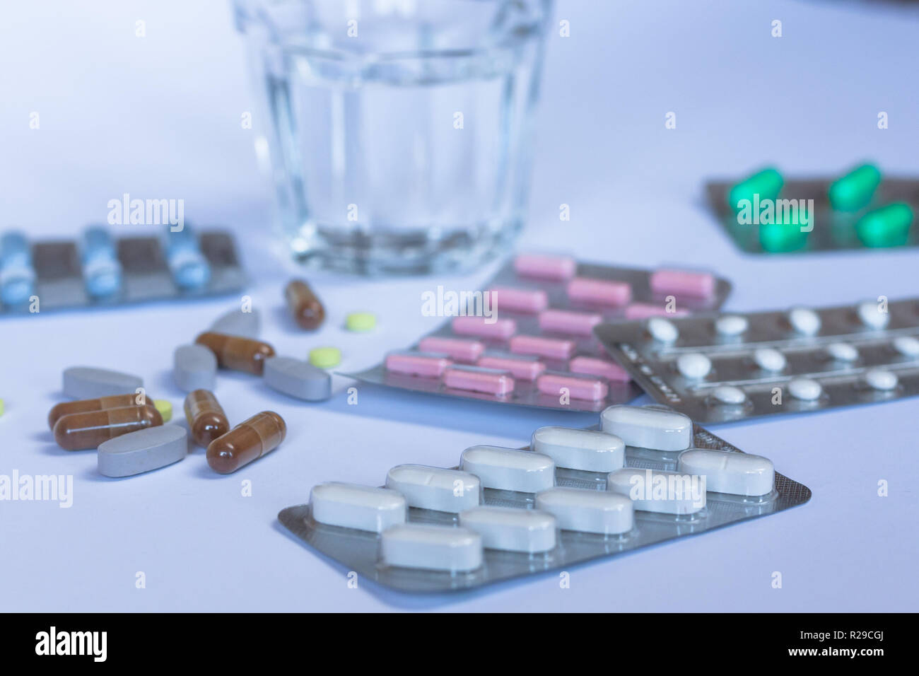 Glass of water and random white, blue, gray, white and magenta pills ...